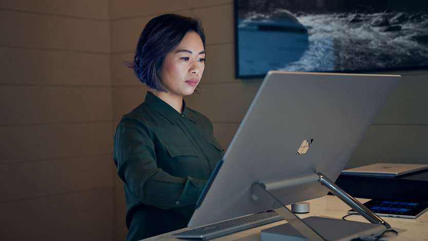 Side profile of a woman wearing a dark shirt in a dim office working on a Microsoft Surface Studio.