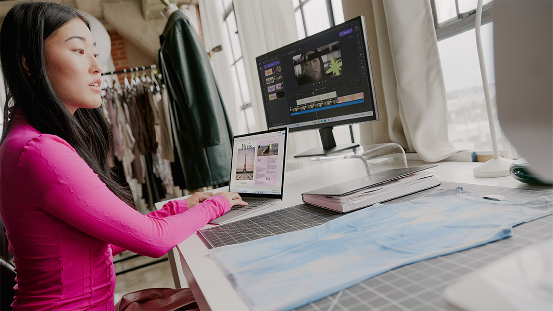 A woman at a desk with two computers, using Microsoft Edge battery saver performance settings